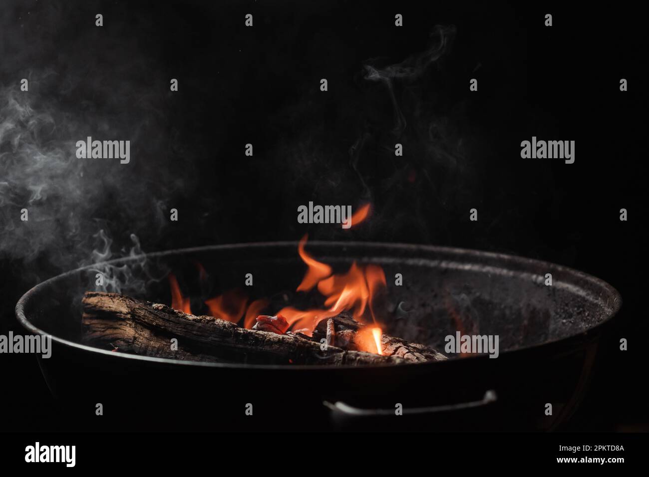 Firewood burns in a round barbecue at night. Dark background. Preparing ...