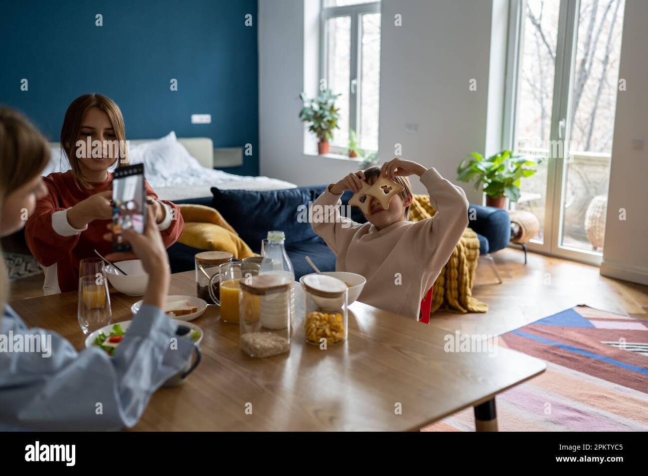 Pleased mom and sister take fun pictures on smartphone as kid boy fool ...