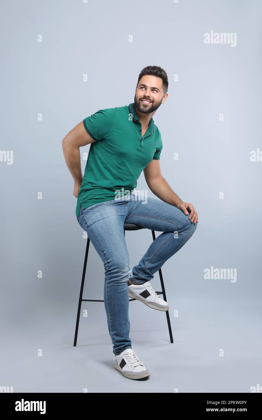 Handsome young man sitting on stool against light grey background Stock ...