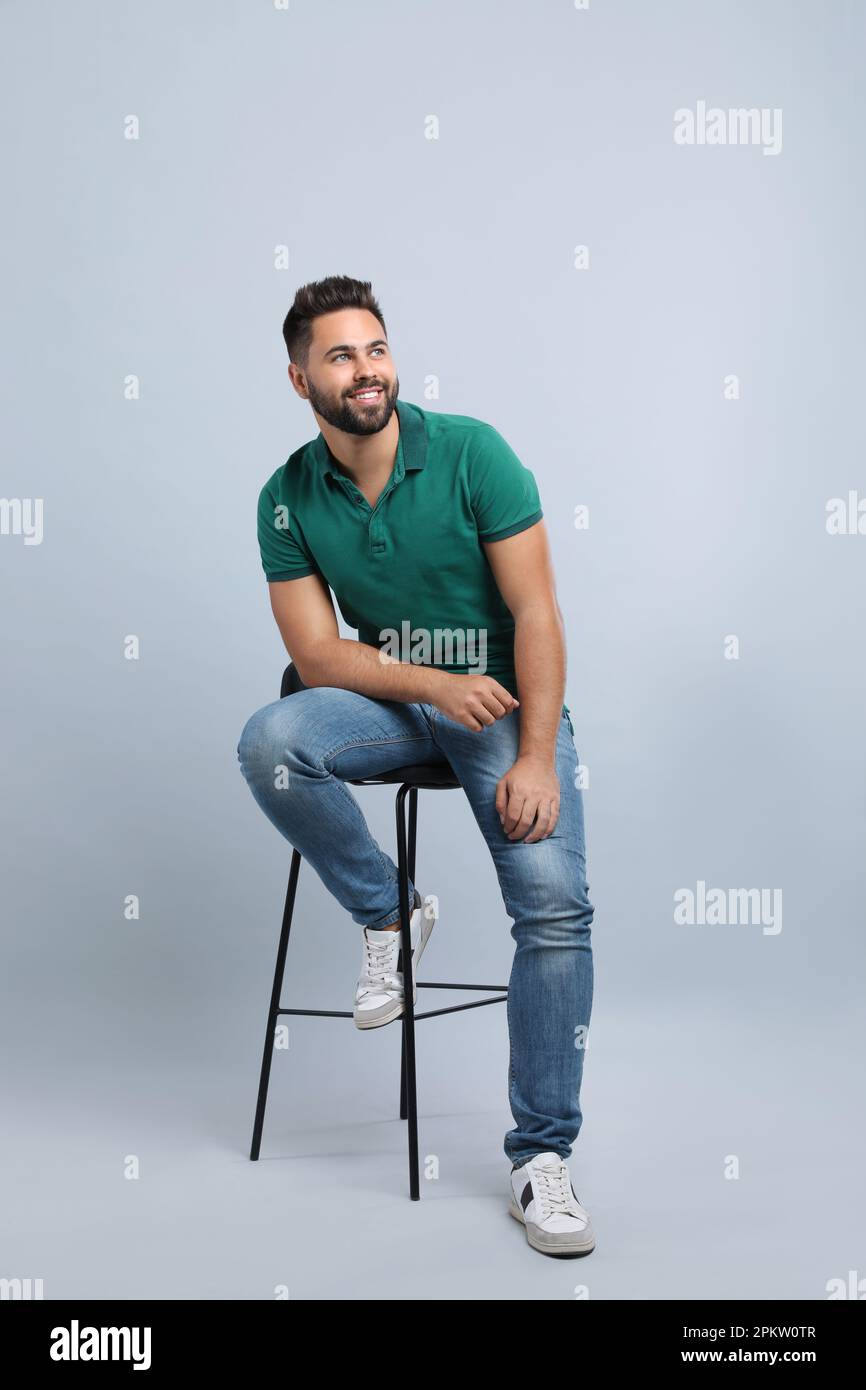 Handsome young man sitting on stool against light grey background Stock ...