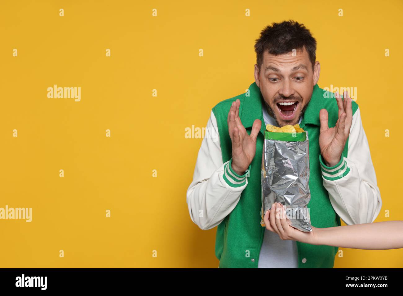 Woman offering tasty potato chips to excited man on orange background ...