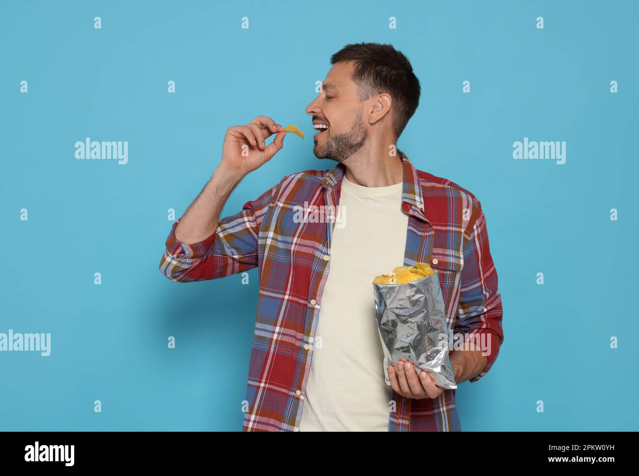 Handsome man eating potato chips on light blue background Stock Photo ...