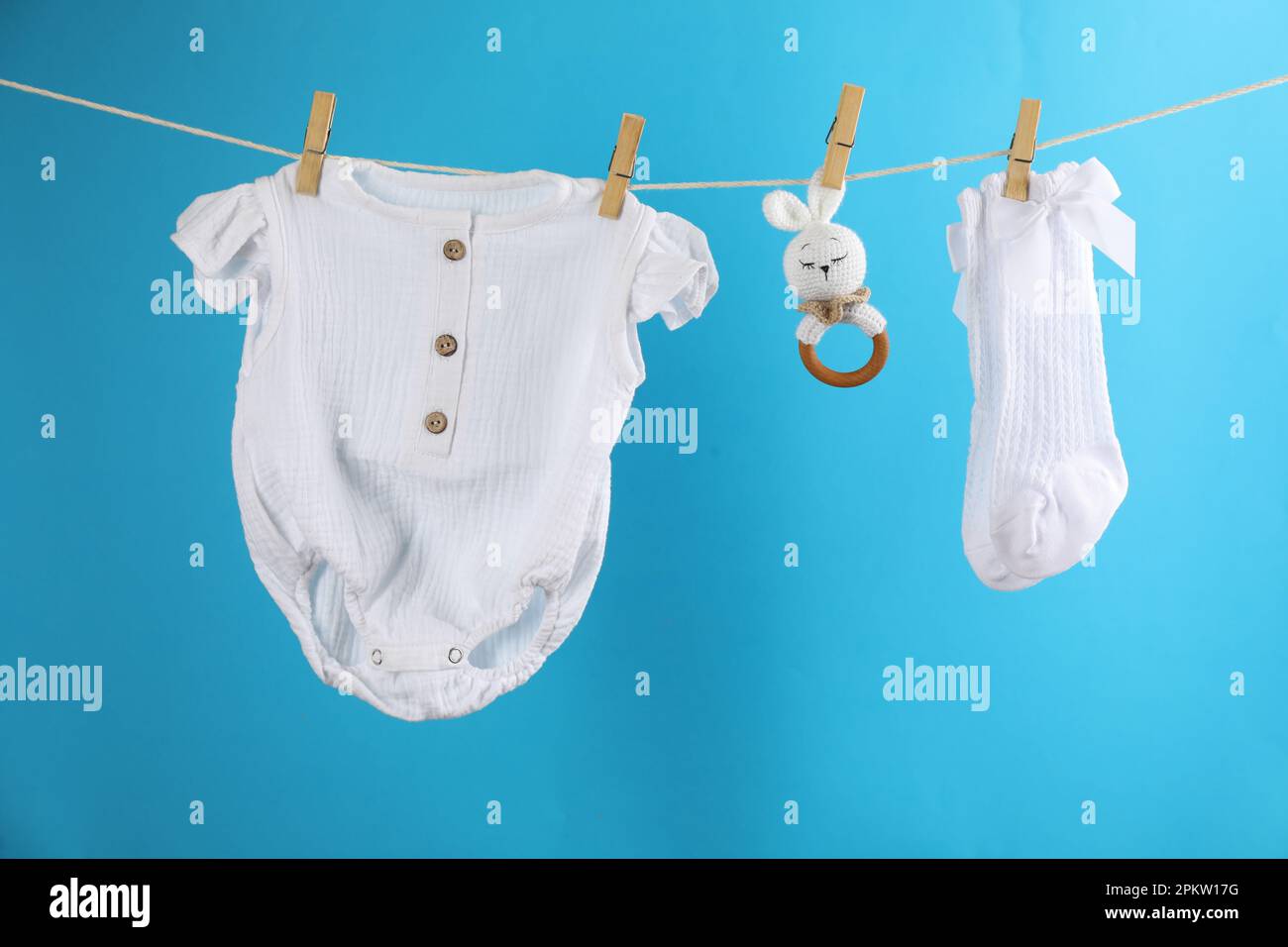 Baby clothes and accessories hanging on washing line against light blue ...