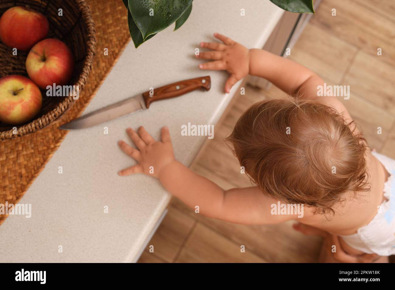 Little child reaching for knife on light countertop, above view ...