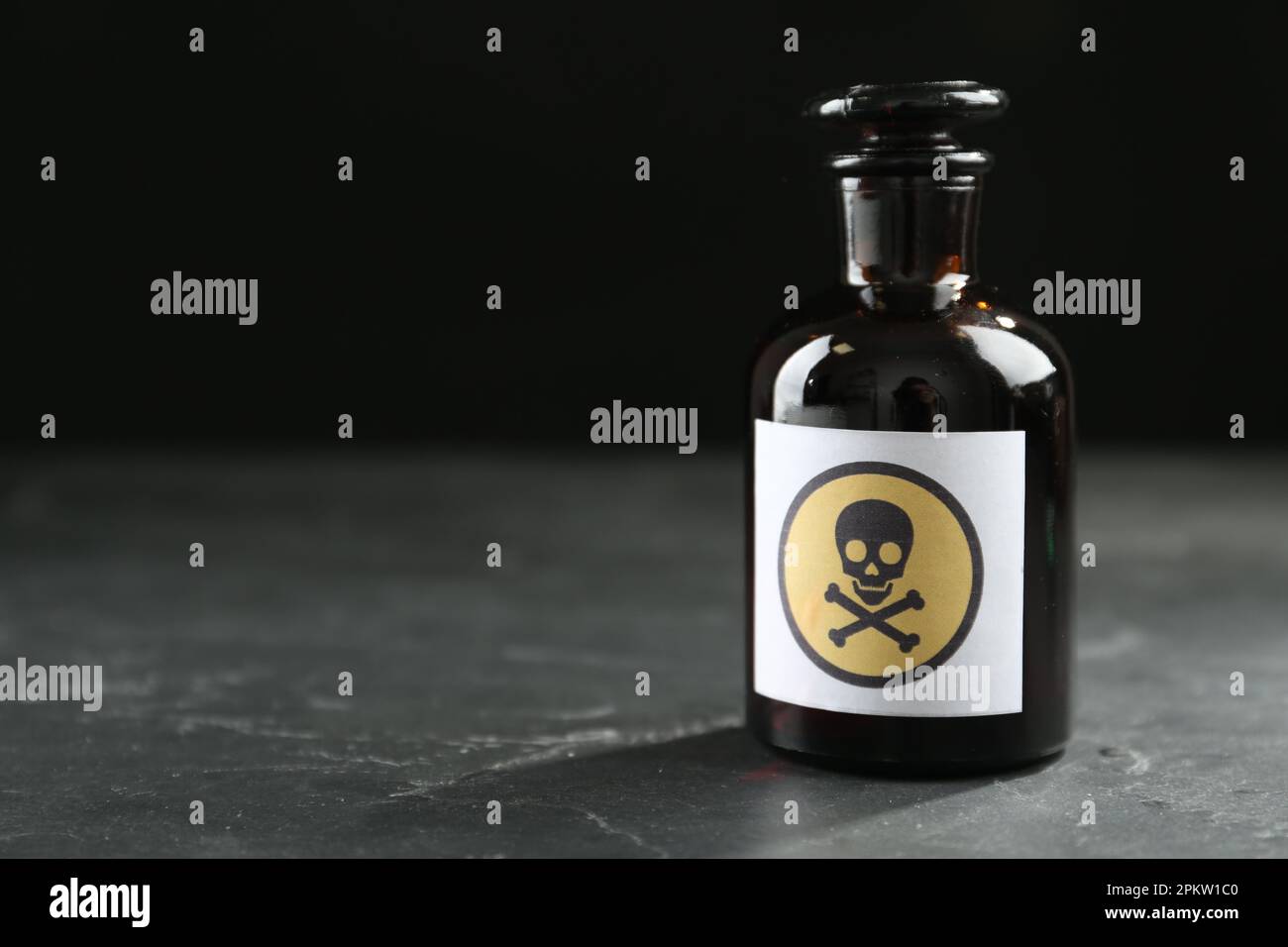 Glass bottle of poison with warning sign on black table. Space for text ...