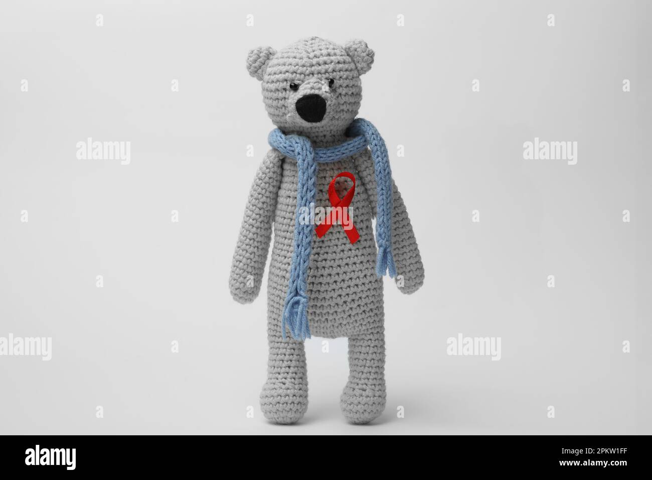 Cute knitted toy bear with red ribbon on light grey background. AIDS ...