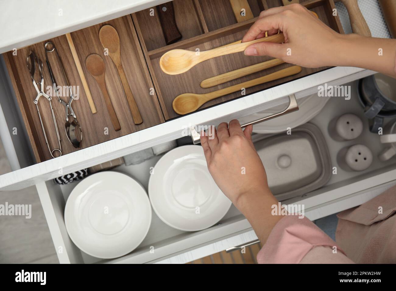 Woman taking wooden spoon from drawer of kitchen cabinet, top view ...