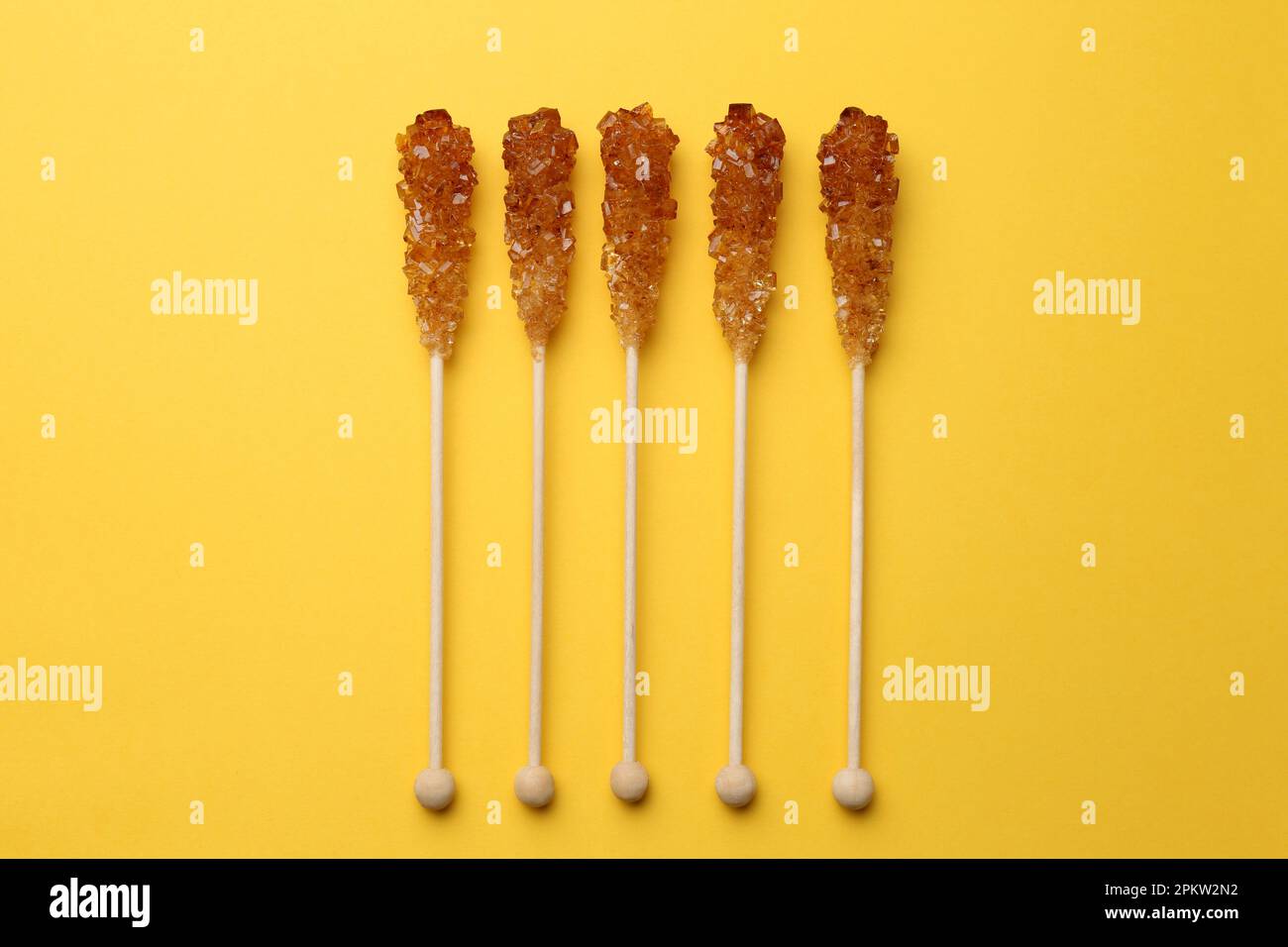 Wooden sticks with sugar crystals on yellow background, flat lay. Tasty ...