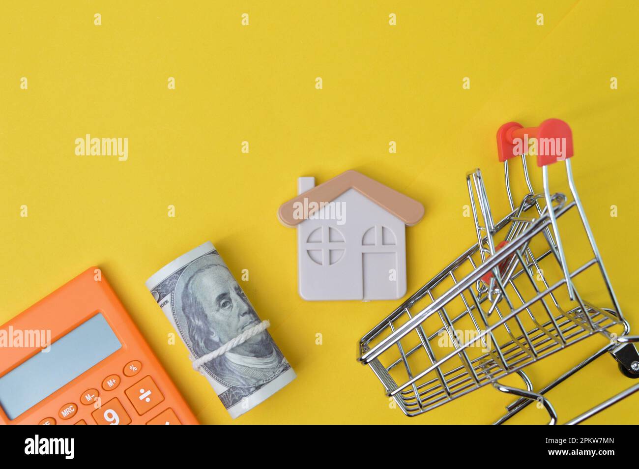 Calculator, toy house, money banknote and shopping cart over yellow ...