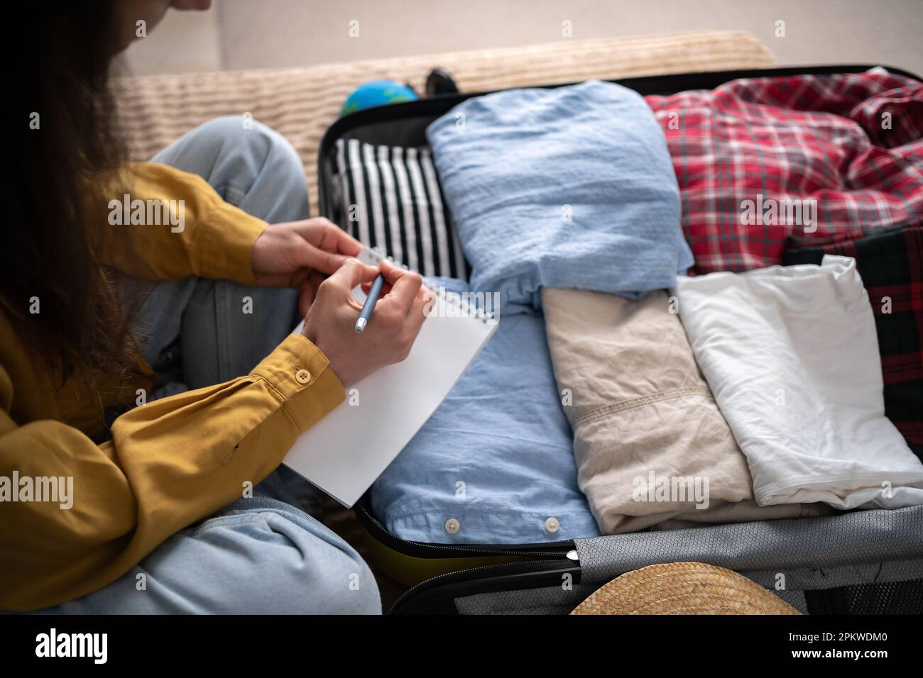 Woman writing checklist before holidays trip. People check clothes into ...