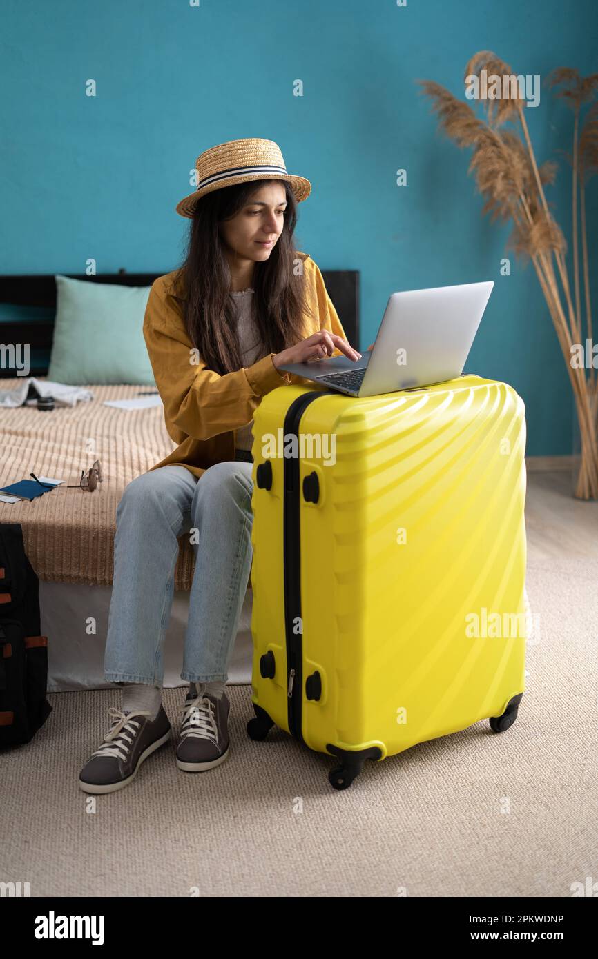 Traveler woman sitting smiling on bed in bedroom with trolley luggage ...