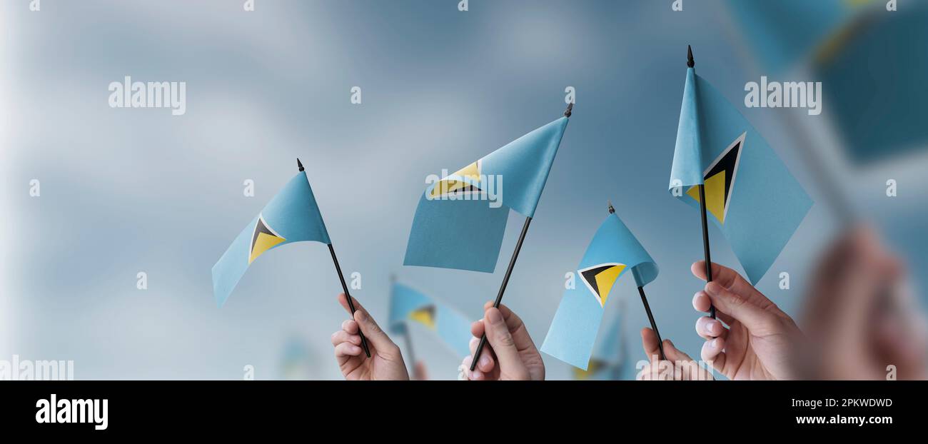 A group of people holding small flags of the Saint Lucia in their hands ...