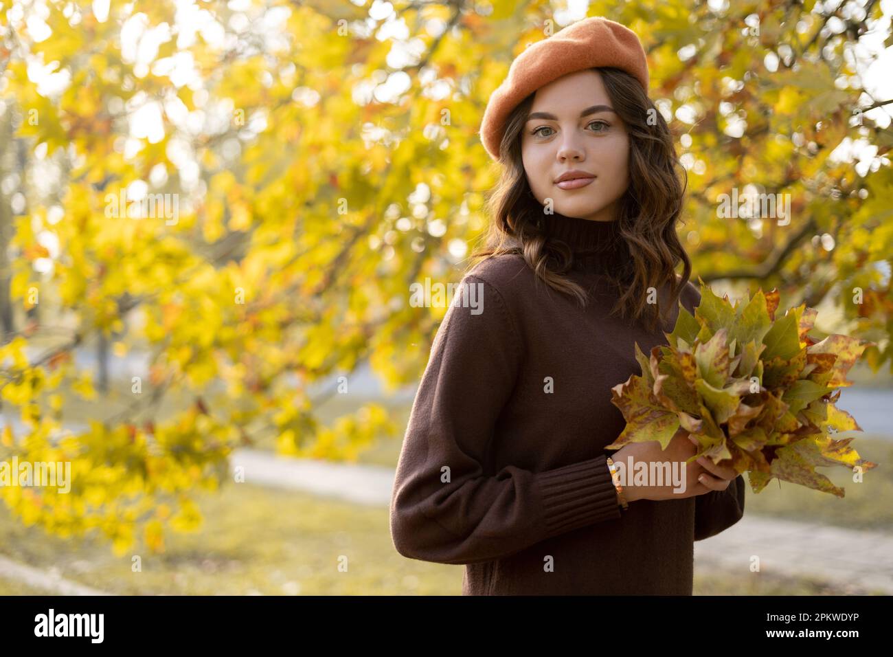 Portrait of cheerful young woman with autumn leaves in front of foliage ...