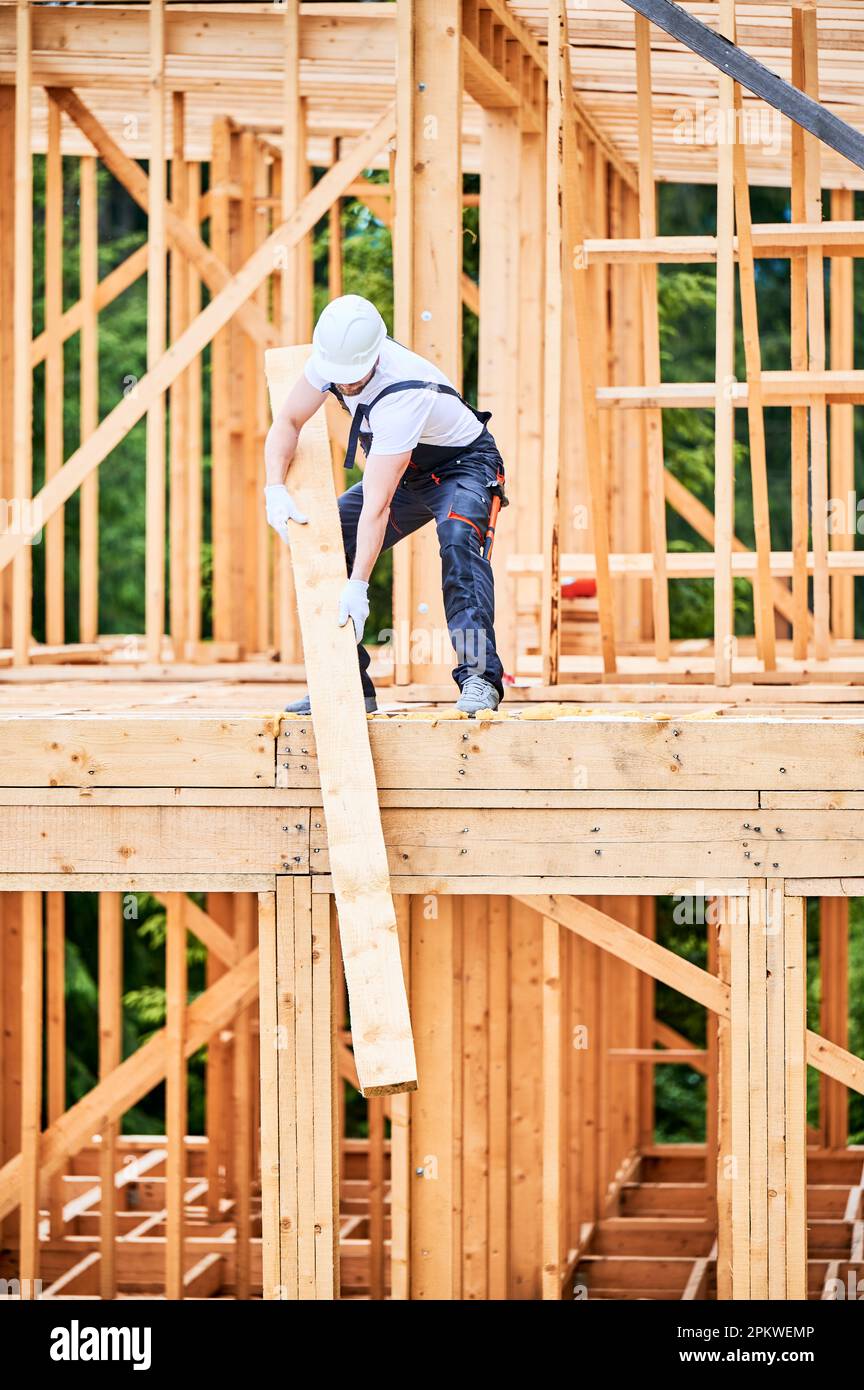 Carpenter building wooden-framed house. Man lifting up large beam ...
