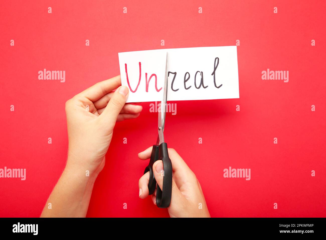 Paper with word Unreal and scissors on wooden table. Hand holding card ...