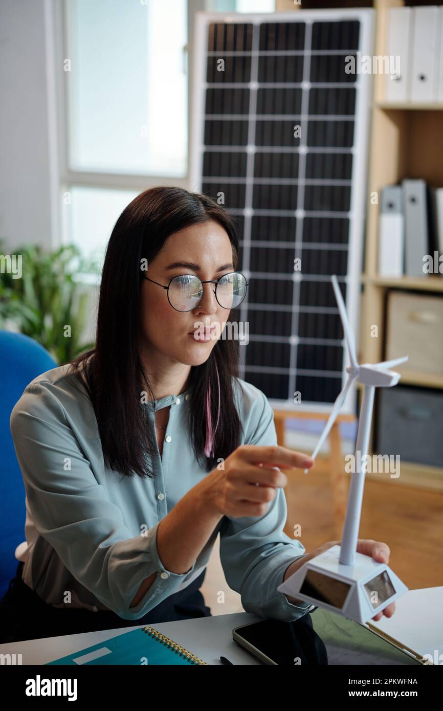 Serious female wind energy engineer looking at model of new wind ...