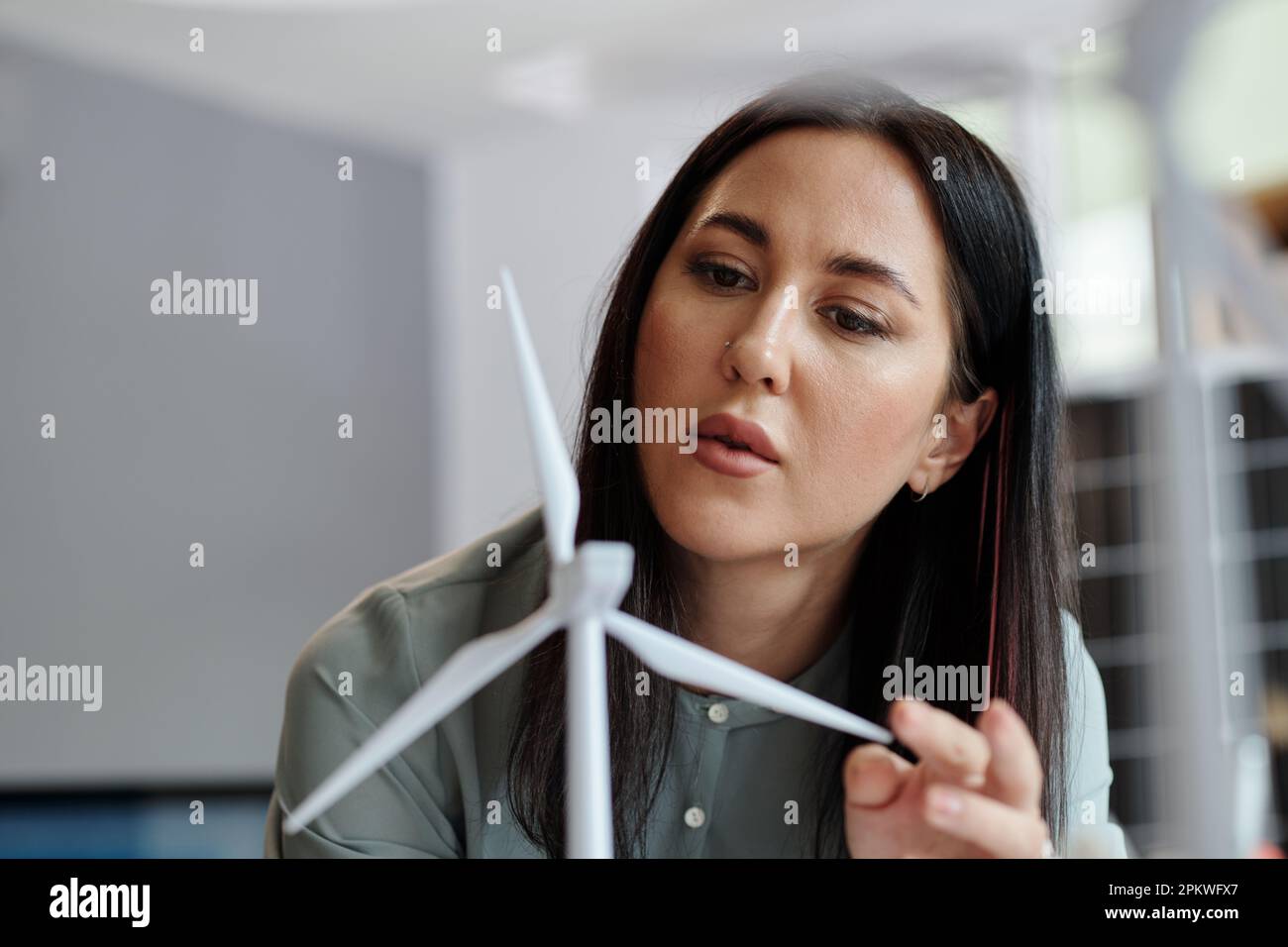 Pensive woman looking closely at model of new innovative wind turbine ...