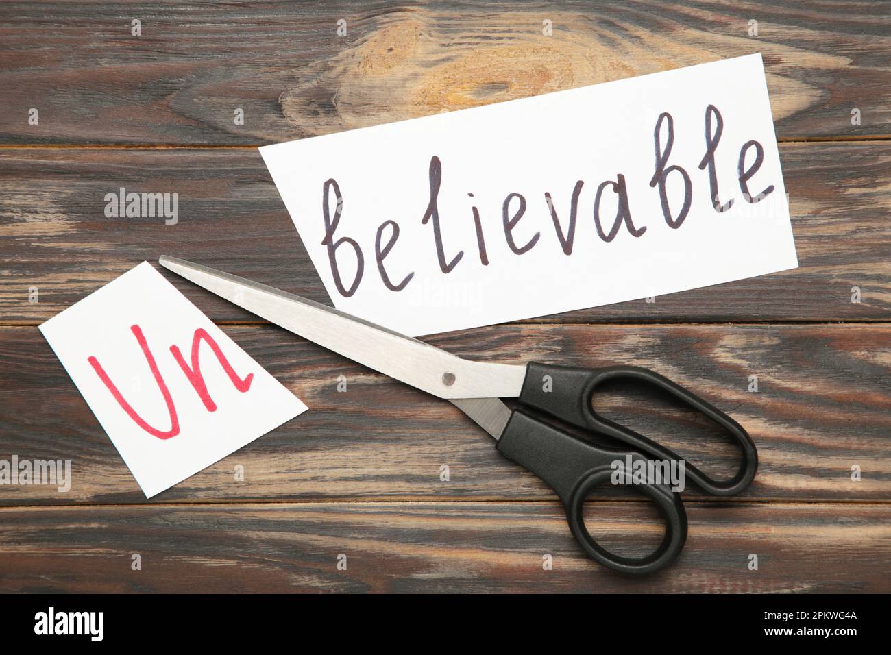 Scissors cutting white paper with the text unbelivable, change word to ...