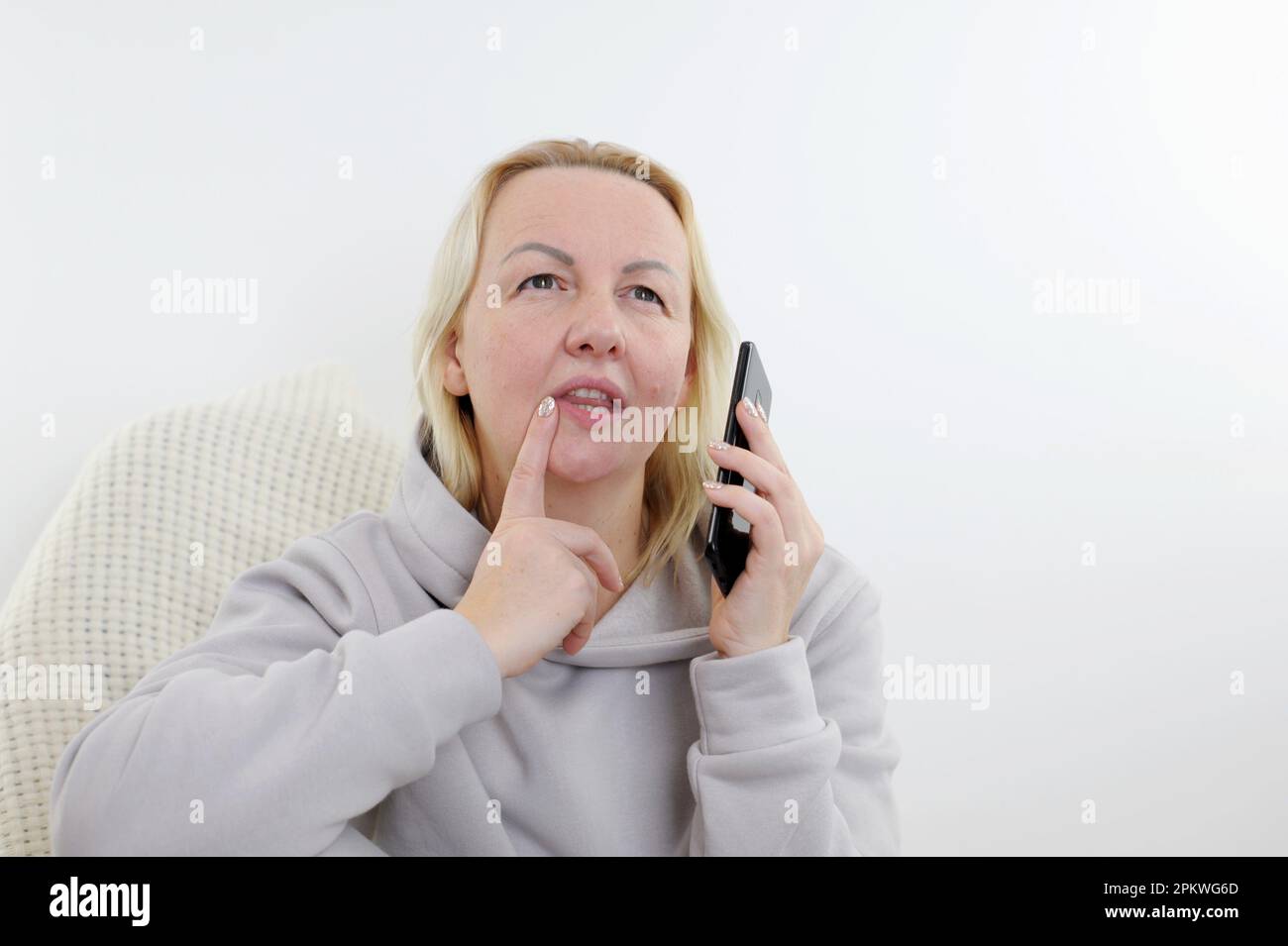 Dreamy middle aged woman resting on couch, holding phone, waiting for ...