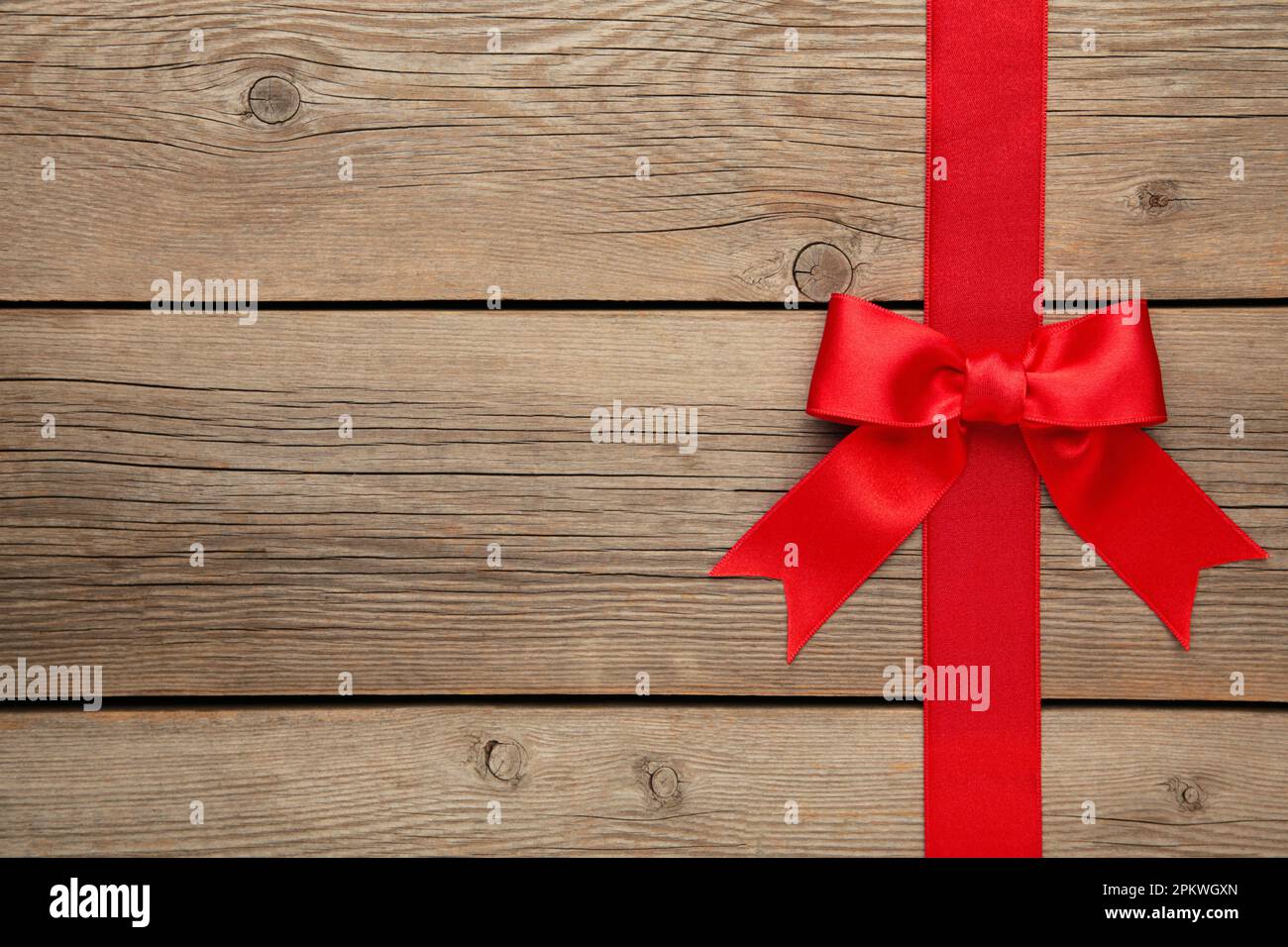 Red ribbon with bow with tails on grey wooden background. Top view ...