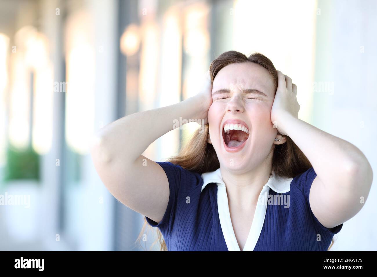 Stressed woman yelling standing in the street with hands on head Stock ...