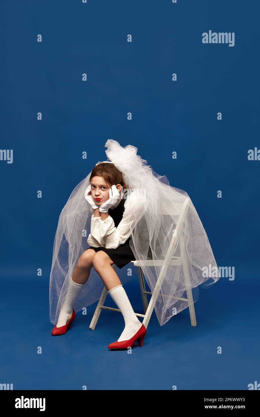 Portrait of young girl wearing brides veil sitting on chair with sad ...