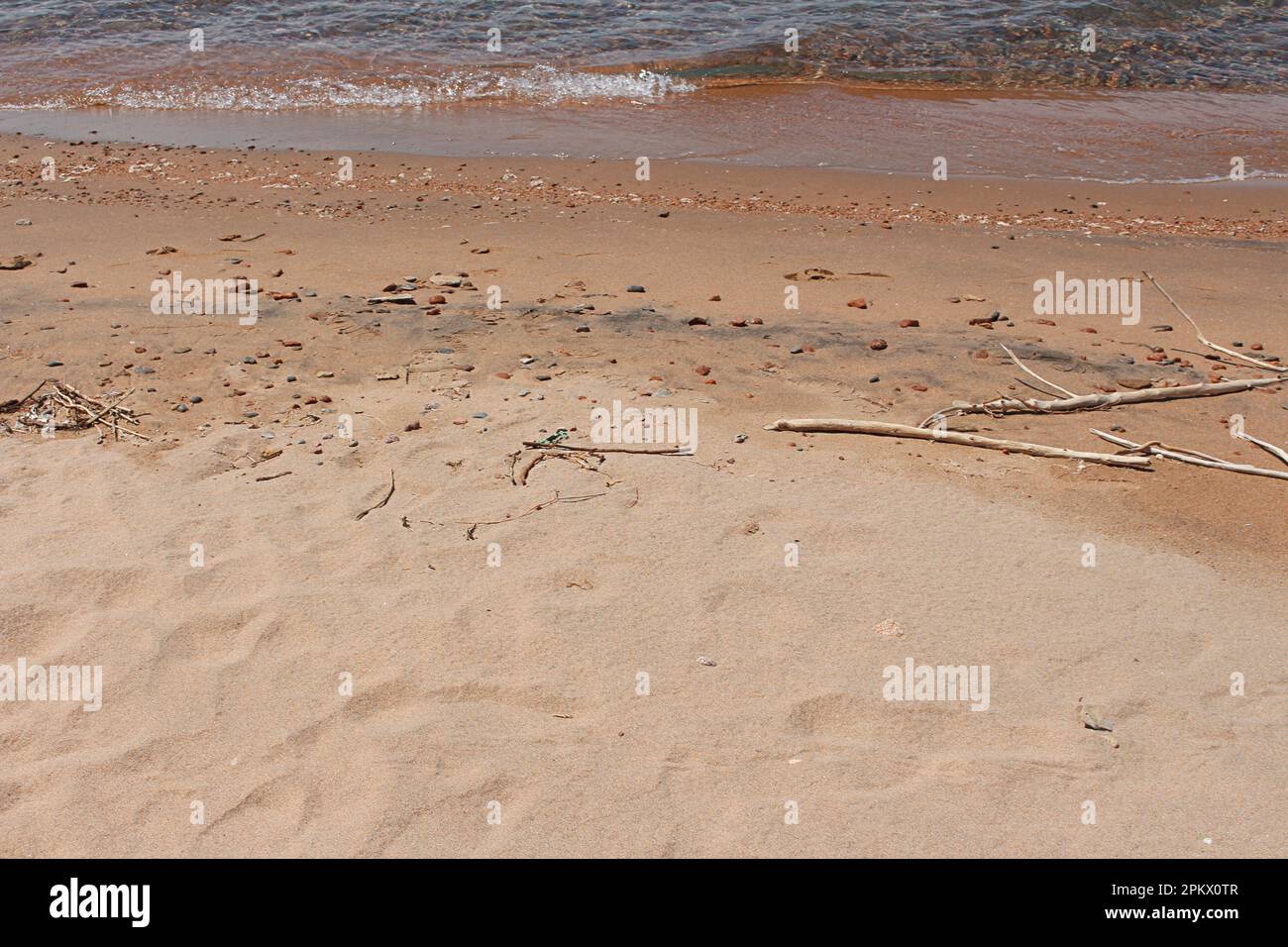 Soft sand on beach with branches and pebbles near water of sea ...