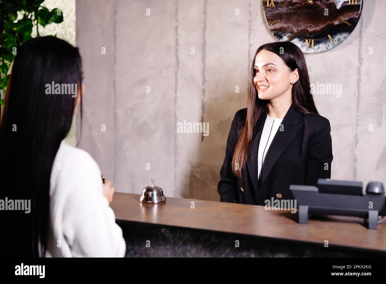 Friendly young concierge standing behind a reception counter talking ...