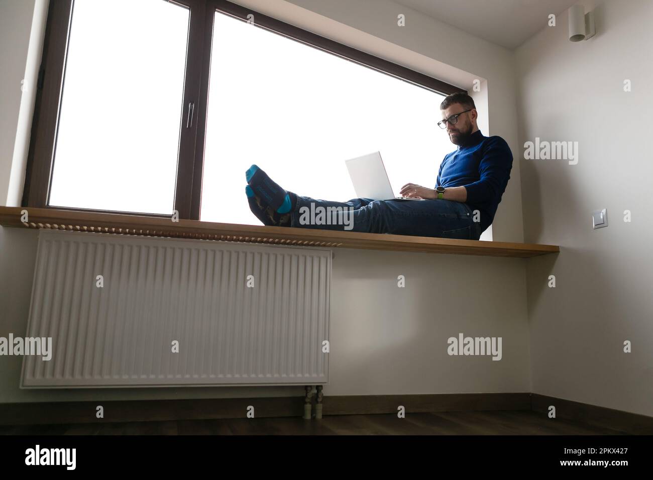 man in blue sweater and jeans is working alone at home with laptop ...