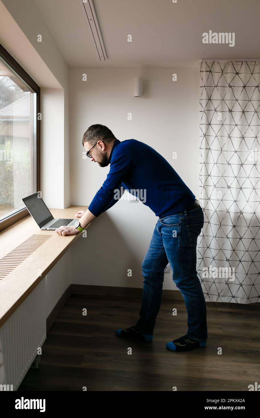 man in blue sweater and jeans is working alone at home with laptop ...