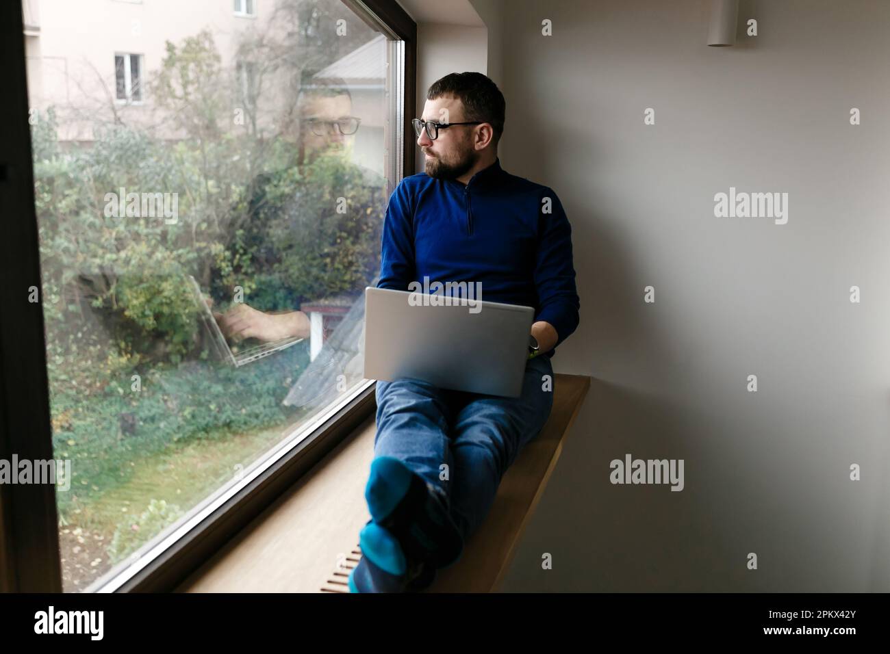 man in blue sweater and jeans is working alone at home with laptop ...
