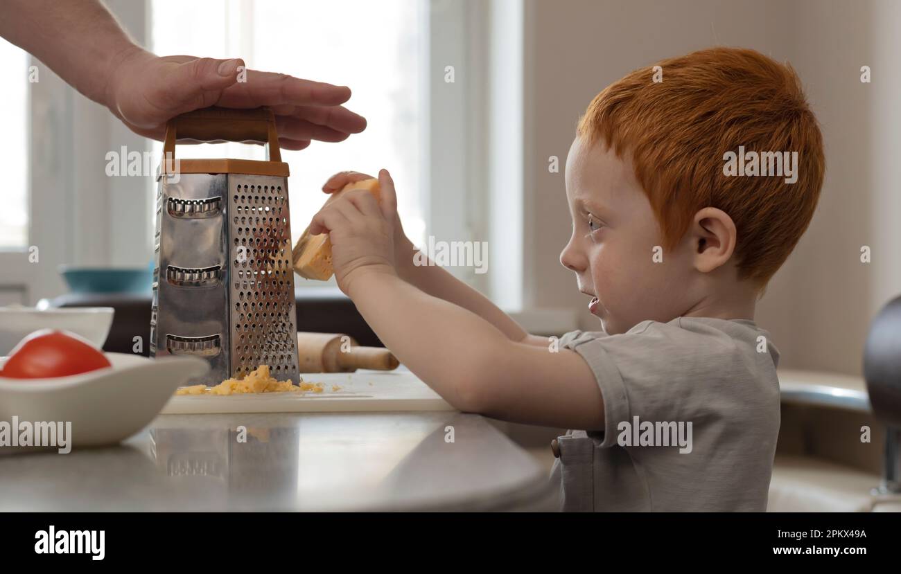 The kid cooks food with his dad, rubs cheese on a grater Stock Photo ...