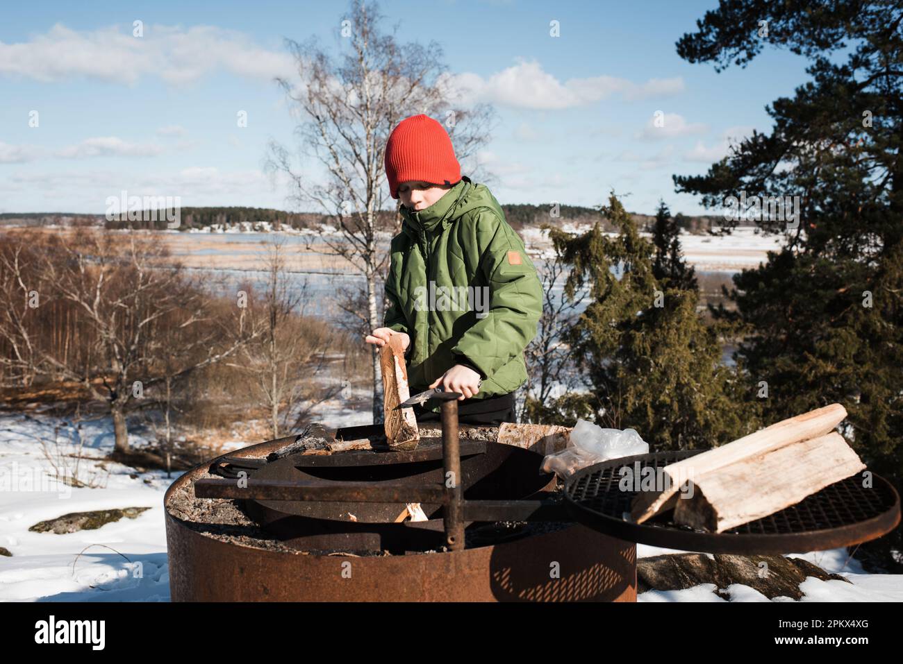 boy using a multitool pen knife taking bark off wood to make a fire ...