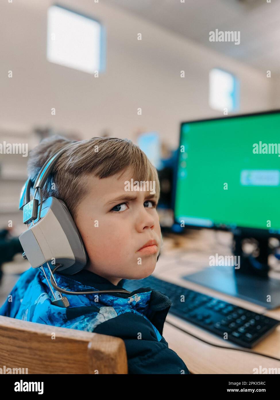Grumpy young kid looking over shoulder with headphones at the computer ...
