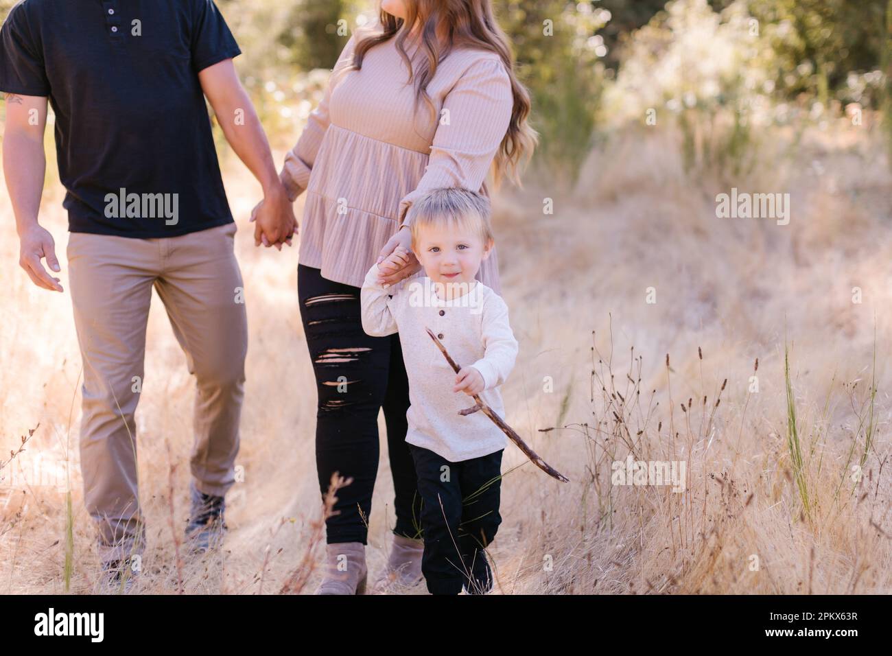 Adorable toddler carrying stick pulling mom and dad Stock Photo - Alamy