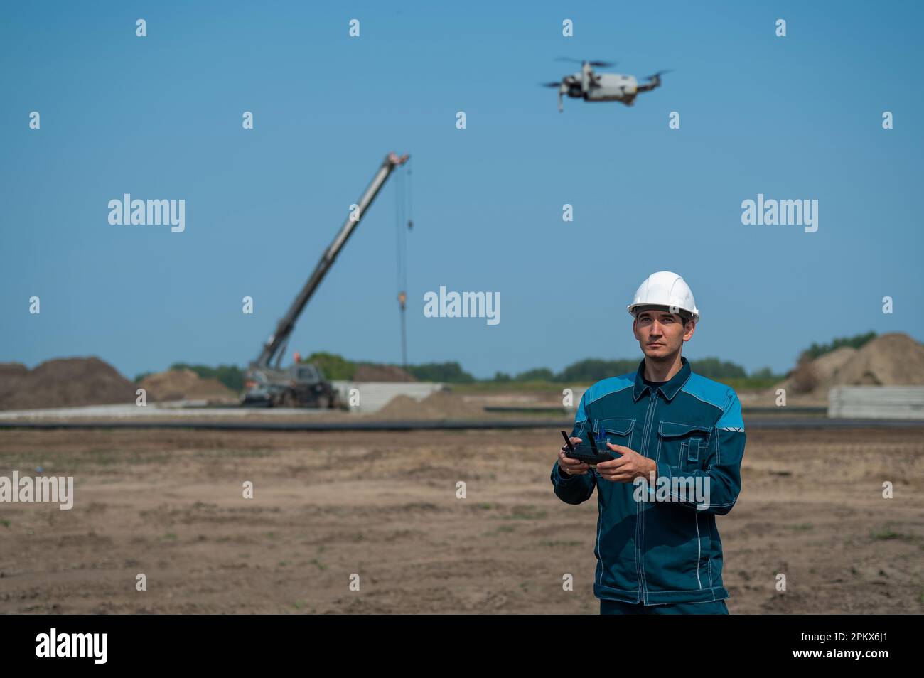 A man in a helmet and overalls controls a drone at a construction site ...