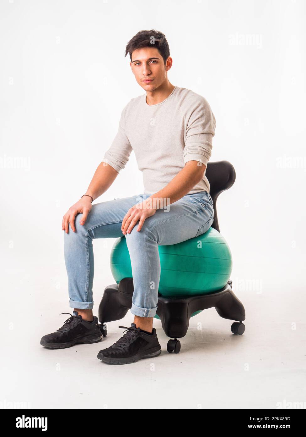 Man sitting on balance ball chair against white background Stock Photo ...