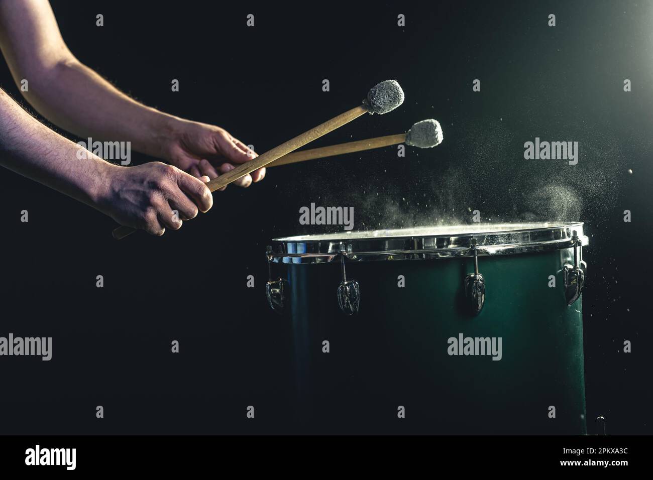 A man plays a musical percussion instrument with sticks on a dark ...