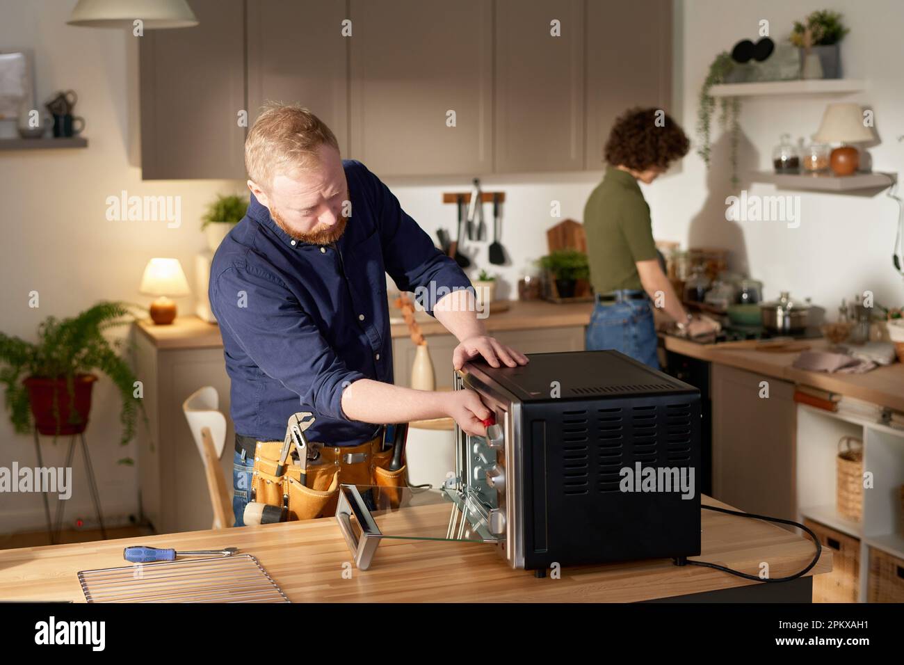 Mature handyman using his work tools to repair oven at home with ...
