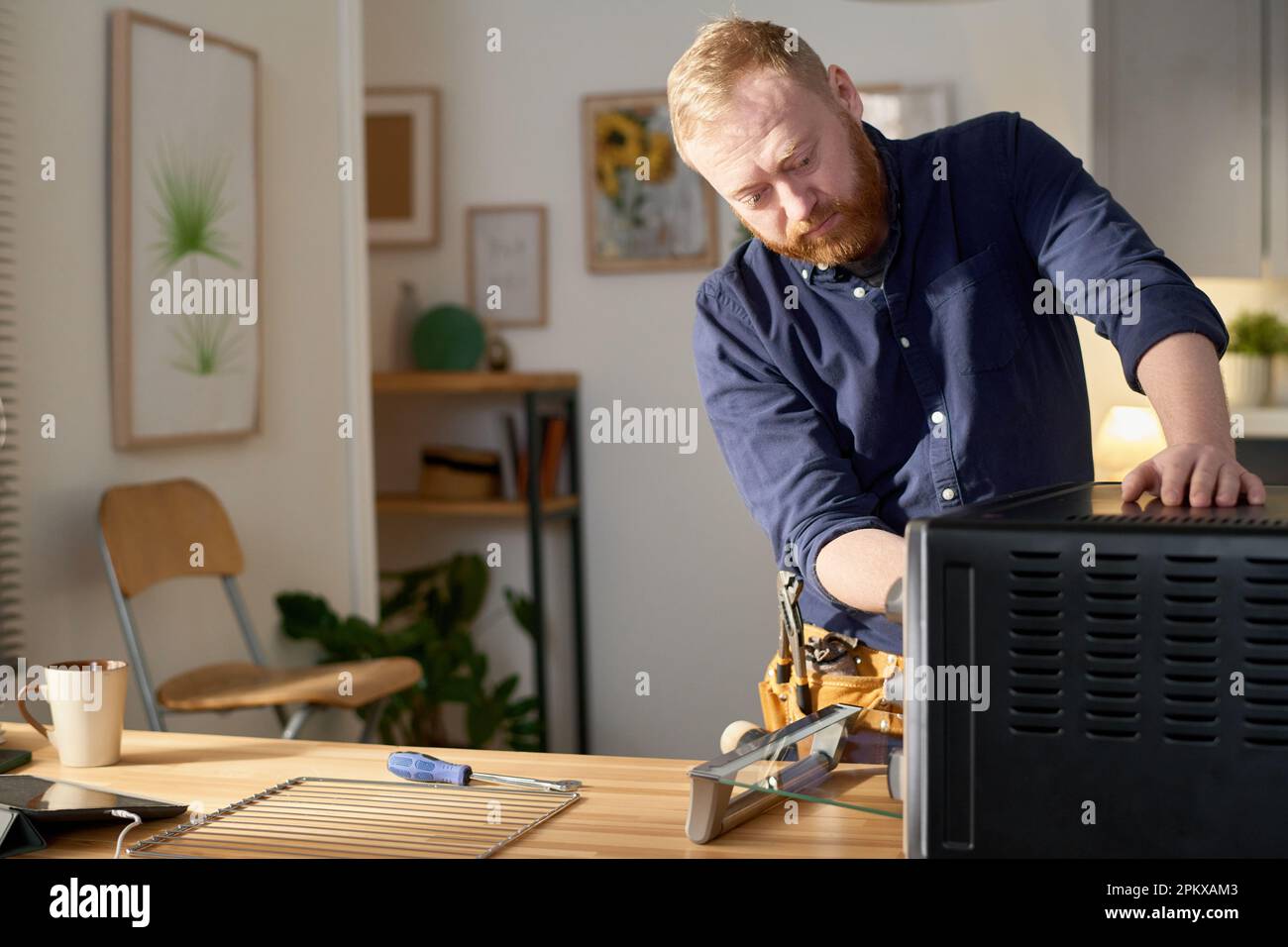 Professional worker repairing broken oven with tools in domestic ...