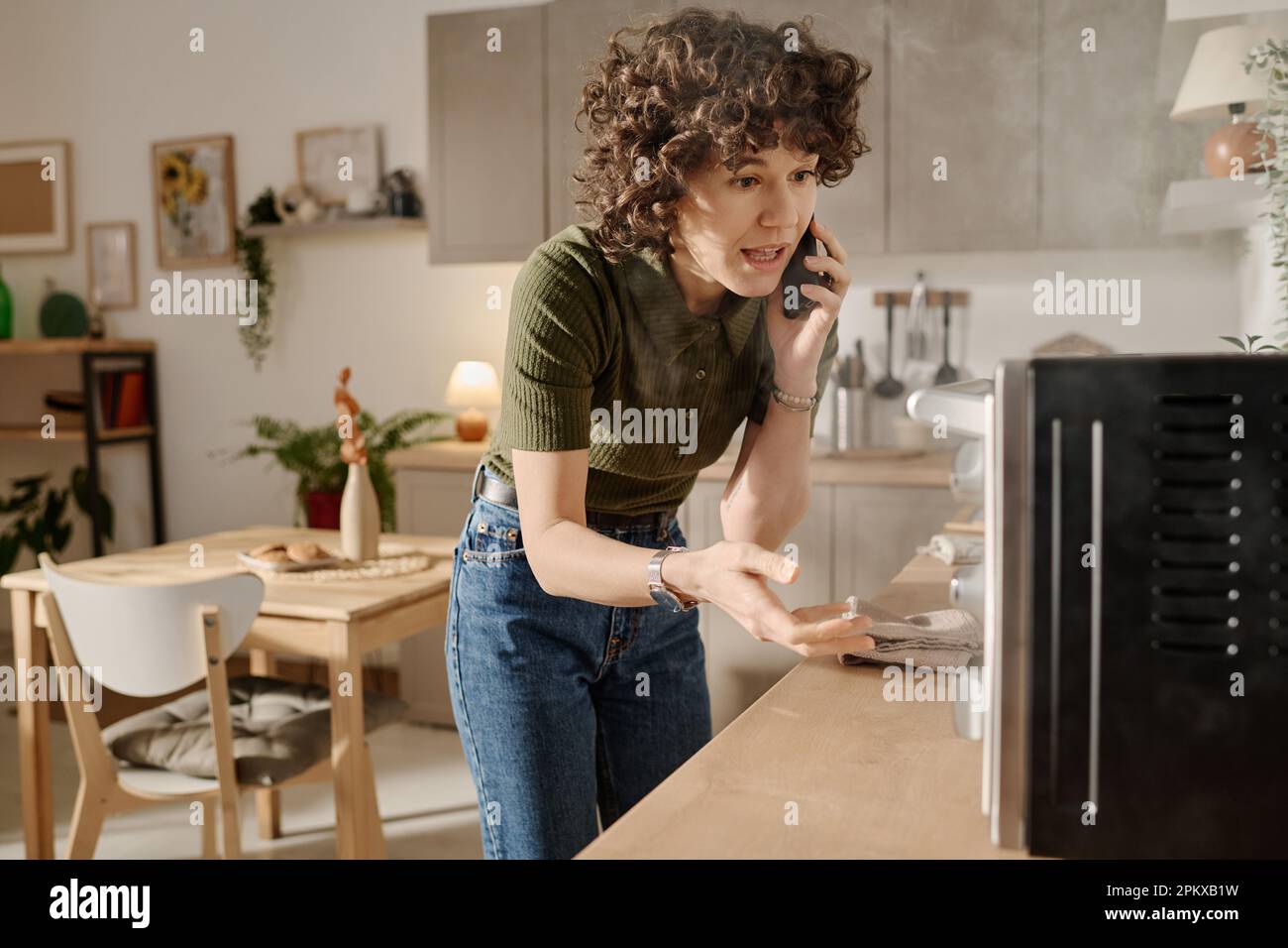 Young woman calling the customer service on breakdown of the oven ...