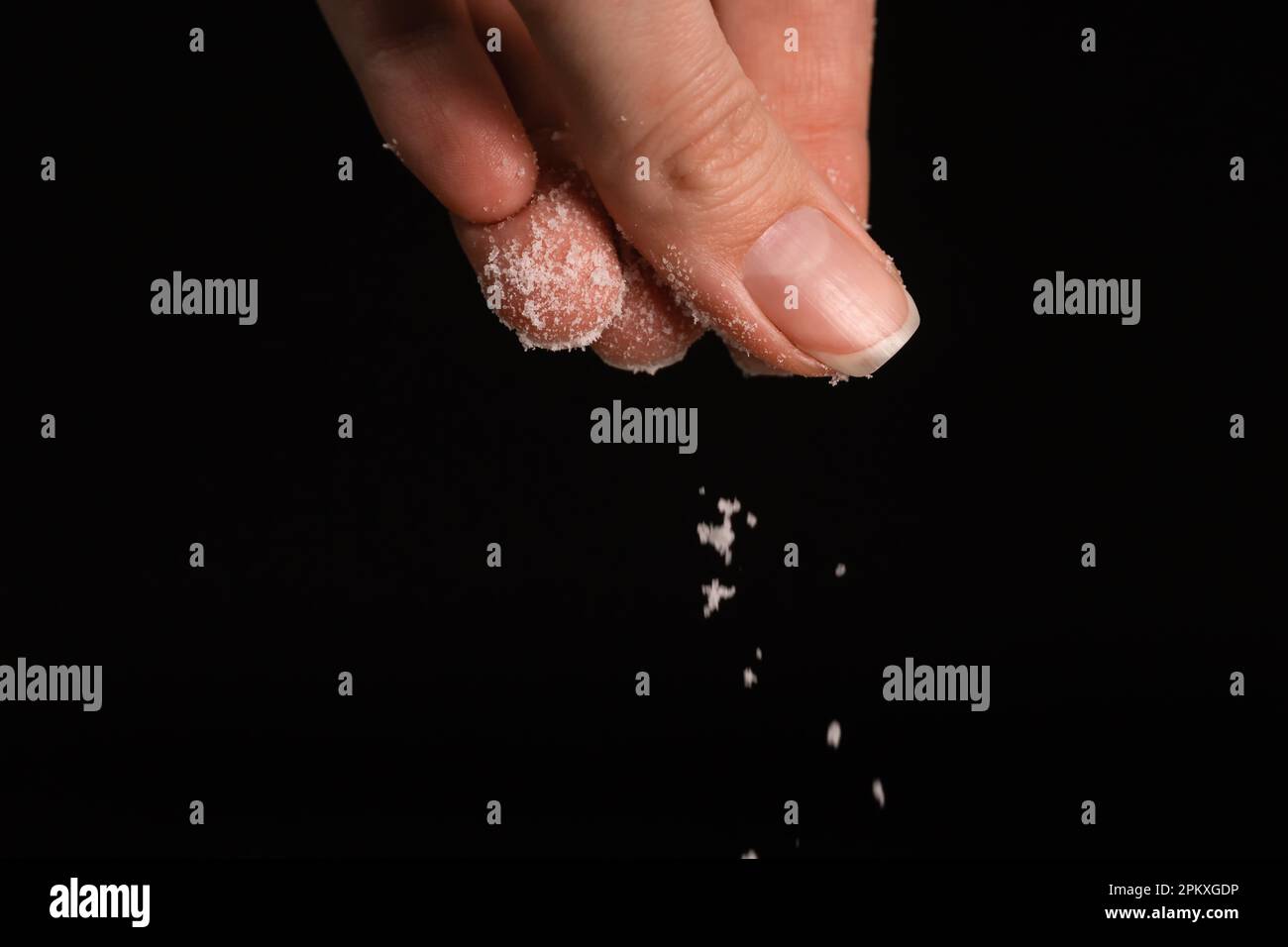 Female fingers sprinkle salt on a black background, copy the space ...