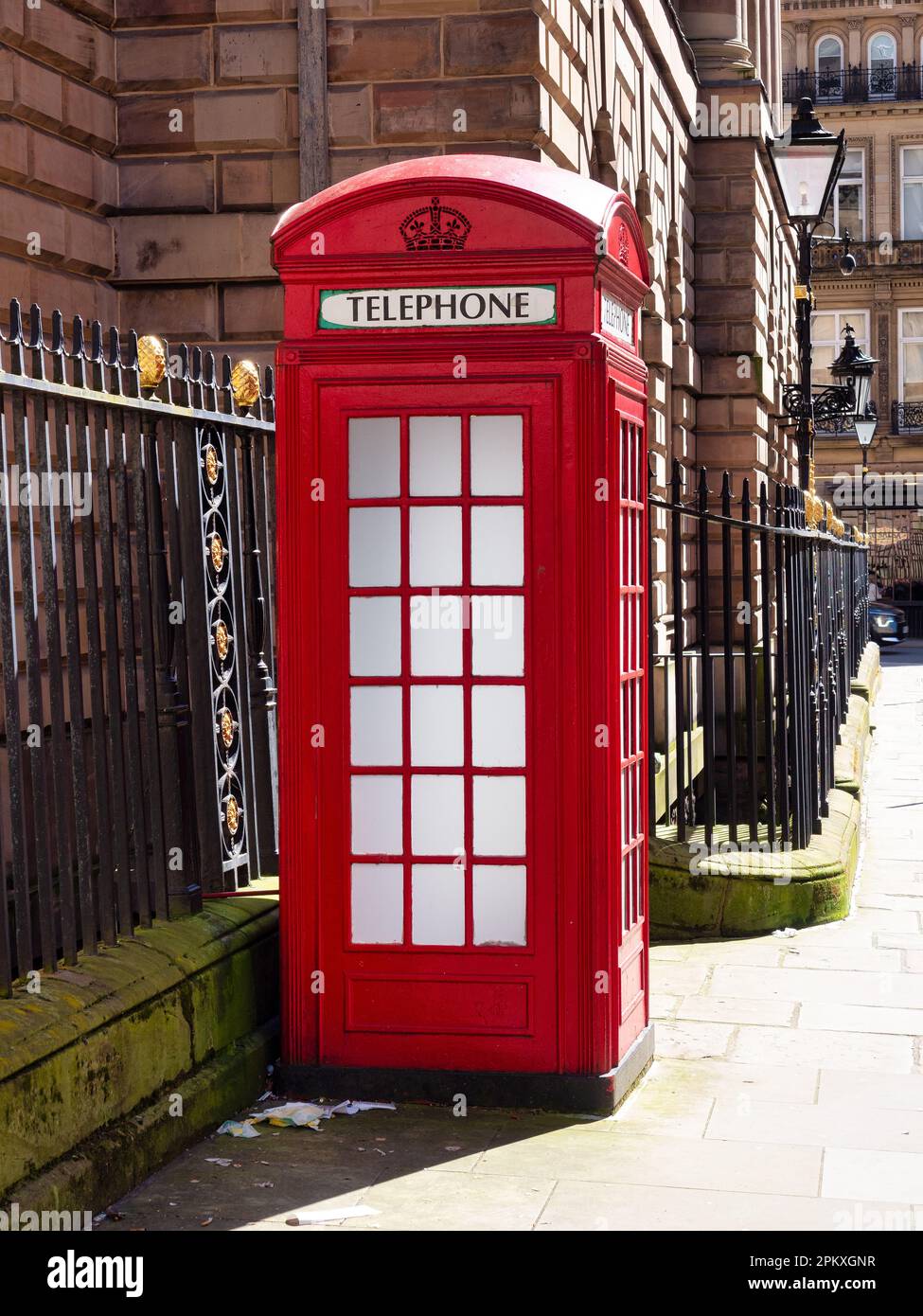 This red telephone box stands against the backdrop of an urban area, a ...