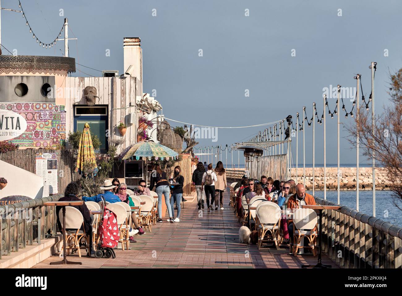 terrace full of tourists eating, sitting on the chairs and the table in ...