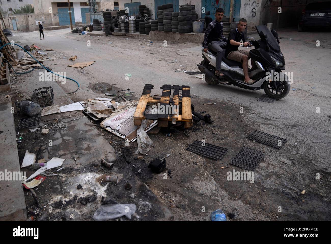 Palestinians on a motorcycle drive past burnt objects at the site of ...