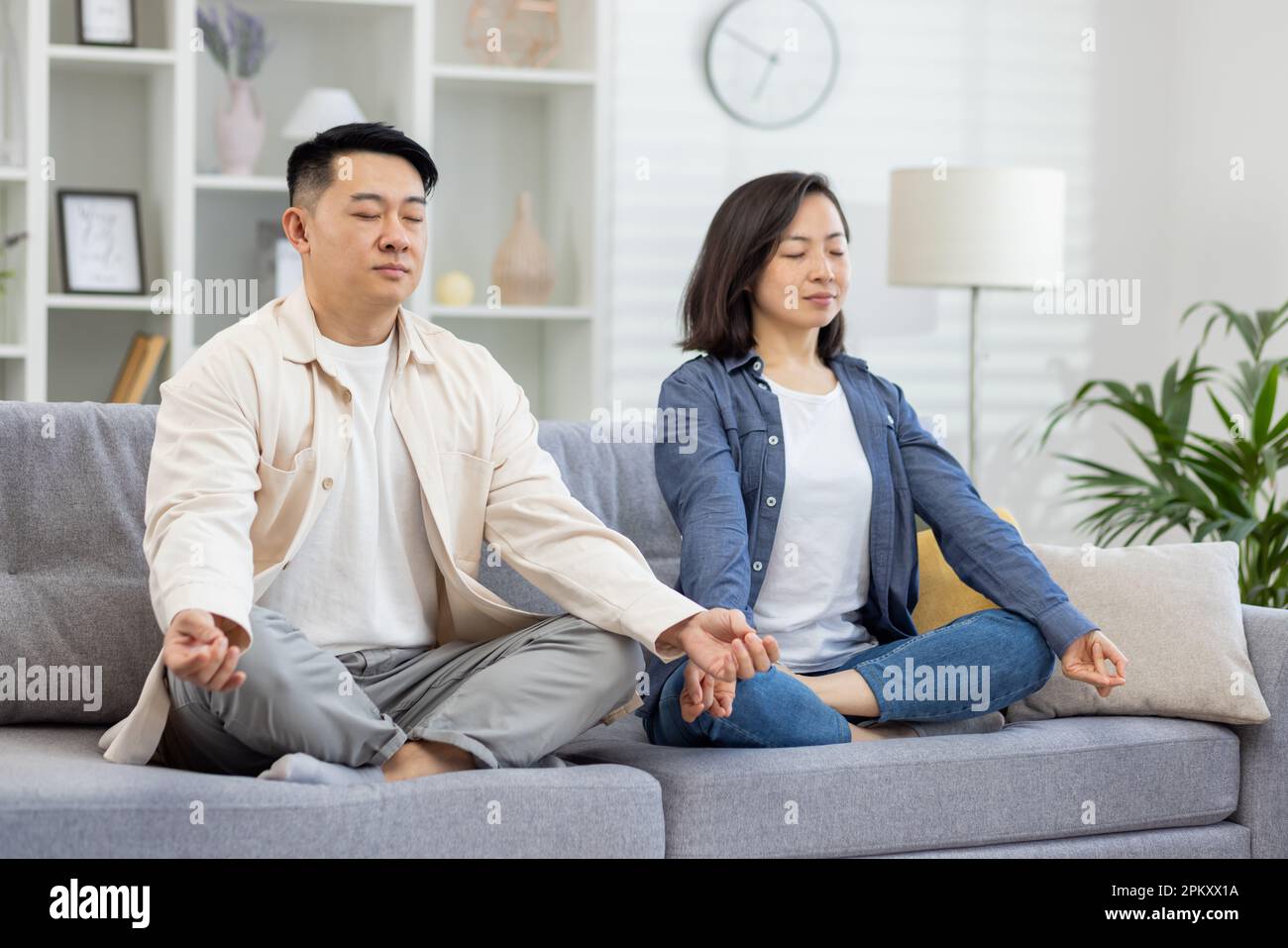 Happy asian family at home on sofa meditating, couple man and woman ...