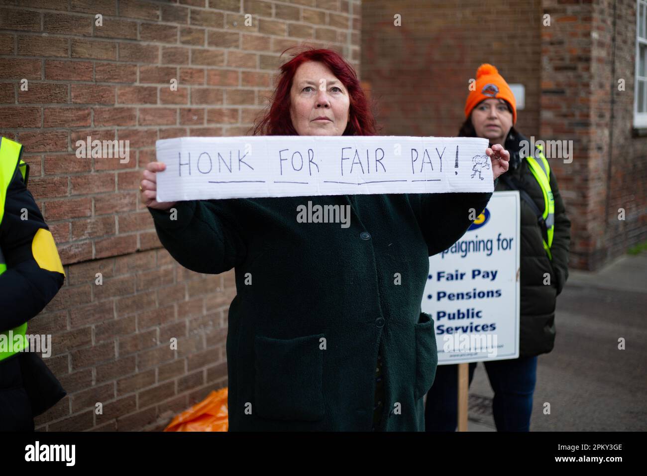 A woman holds a 'Honk for Fair Pay' banner at an official picket line ...