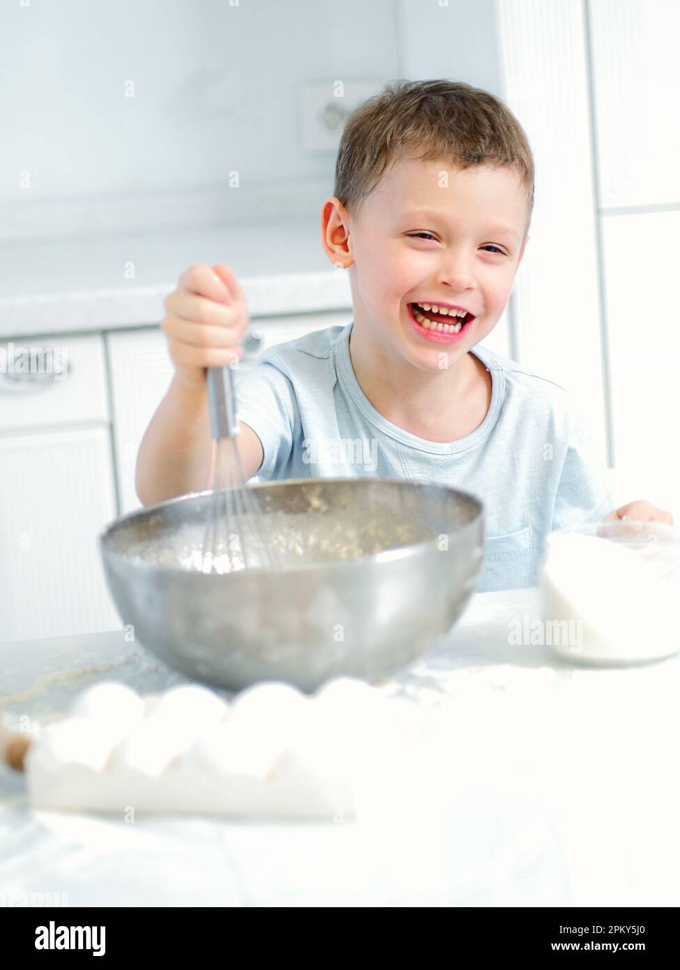 Child cooks food. Caucasian boy sits at table in kitchen and kneads ...