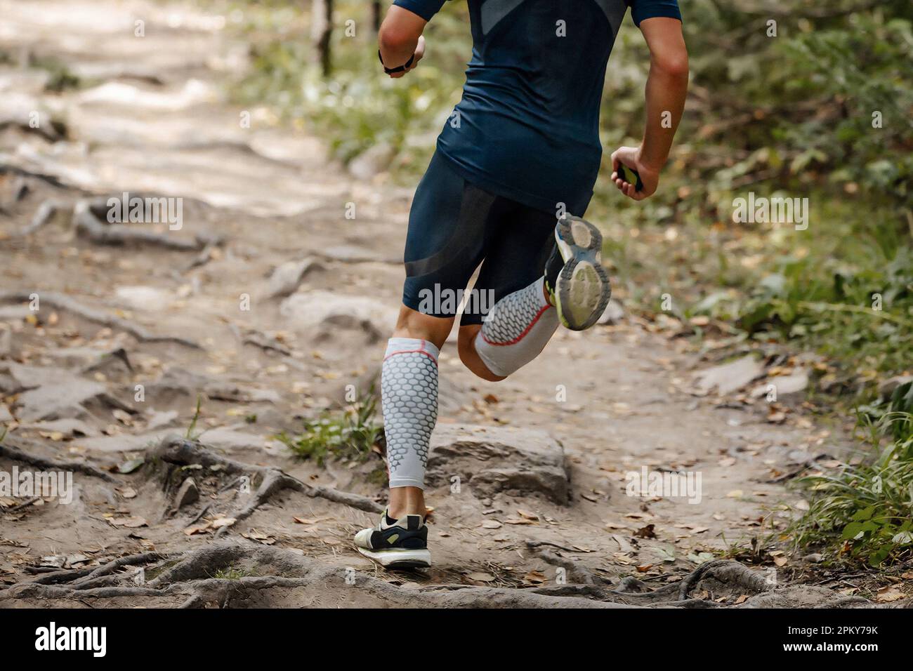 back athlete runner in compression sleeves on his feet running forest ...