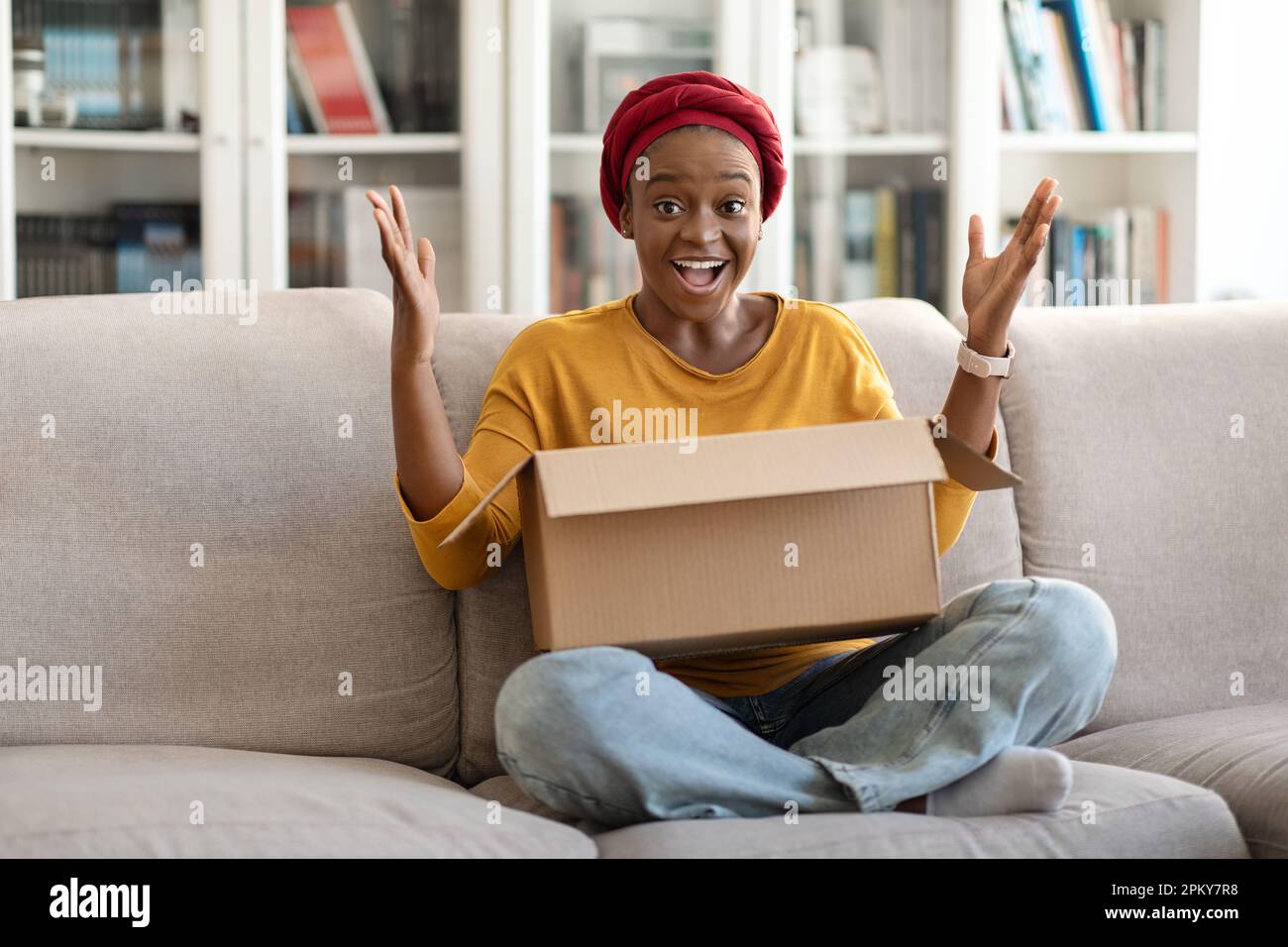 Emotional young black woman unpacking parcel at home, gesturing Stock ...